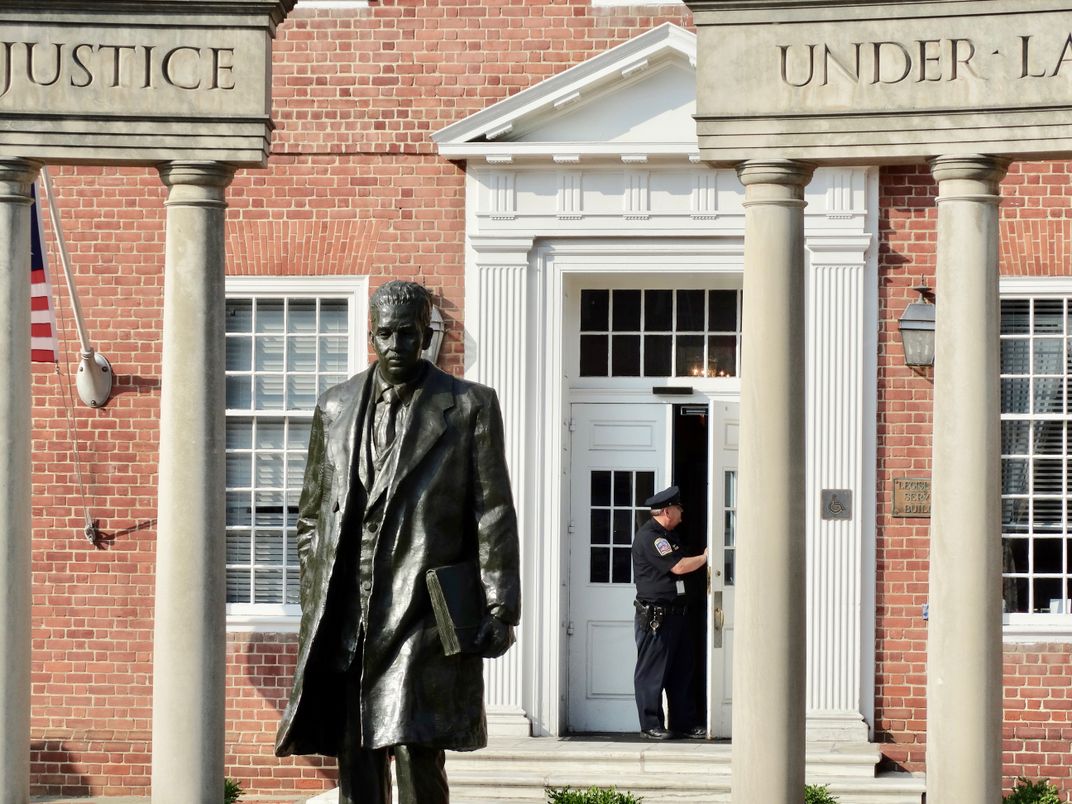 Police officer entering state office building behind statue of first ...