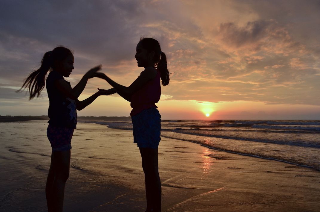 Two little girls play clapping on the beach at sunset | Smithsonian ...