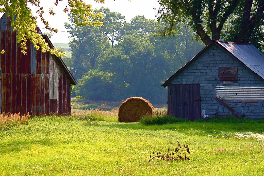A Round Bale of Hay between an Old Shed and an Old Barn; drying in the ...