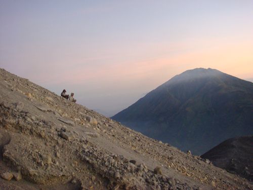 Climbers sit on the side of Mount Merapi looking at other volcanoes ...