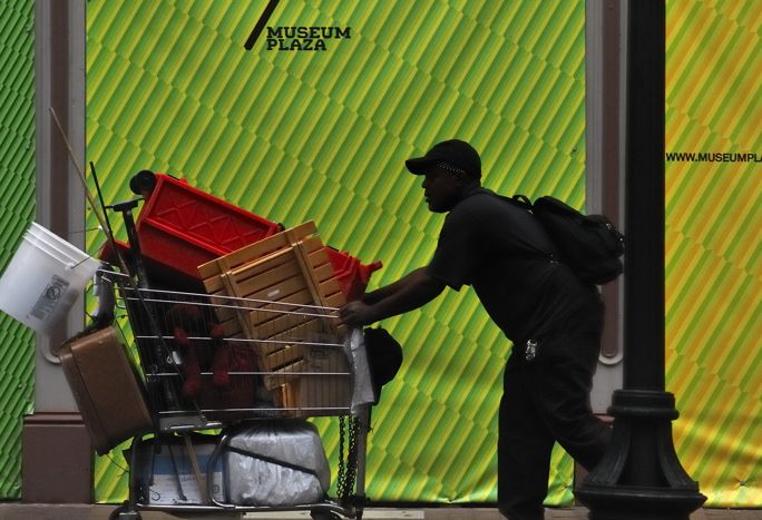 A homeless man pushing a shopping cart past a luxury condo high rise ...