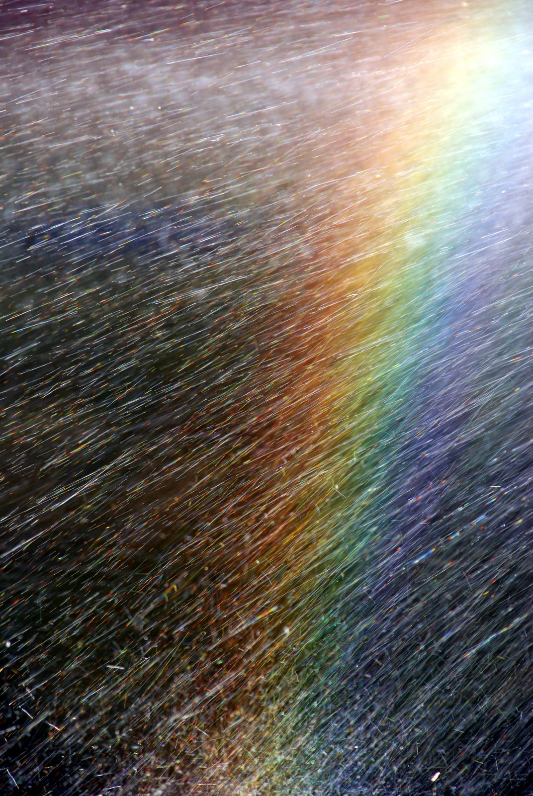 Sunlight playing through the spray of an ornamental fountain creates a ...