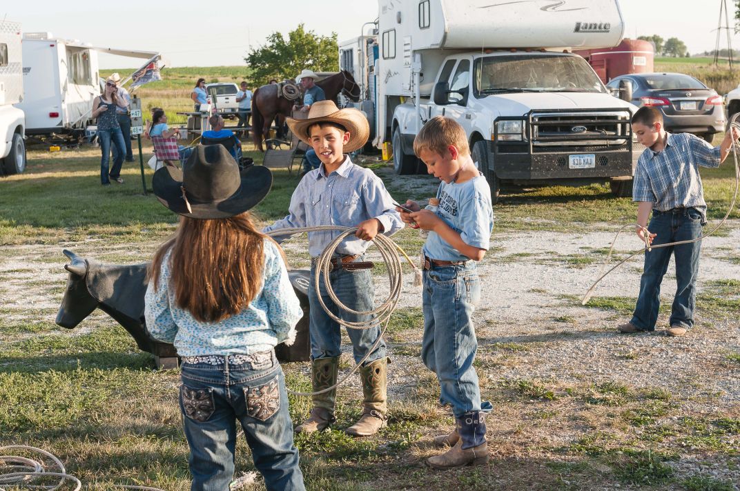 Boys and girls play and practice roping a dummy calf while adults ...