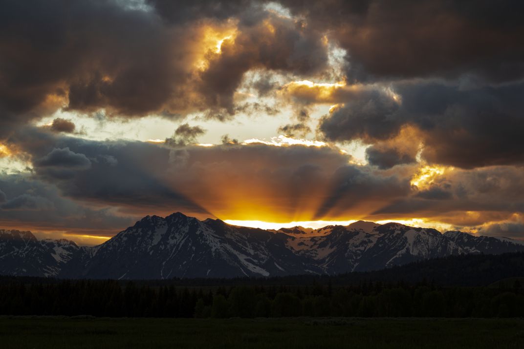 Sun rays peaking over the Grand Teton Mountains during sunset ...