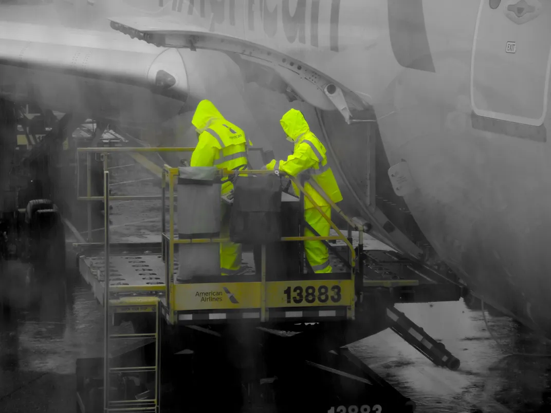 Airport workers loading up a plane in the rain | Smithsonian Photo ...