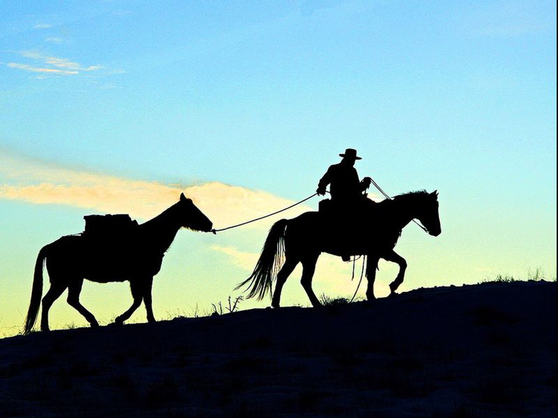 A cowboy and his pack horse are silhouetted against the evening sky as ...