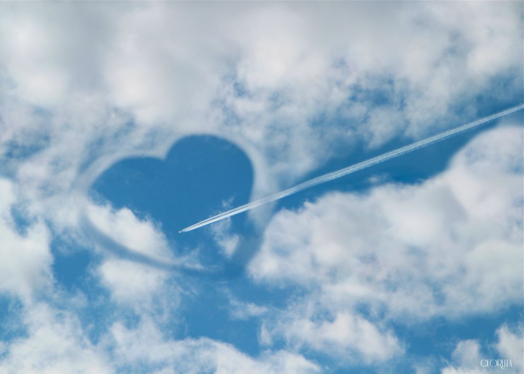A plane flying through a heart shaped cloud creating the arror ...