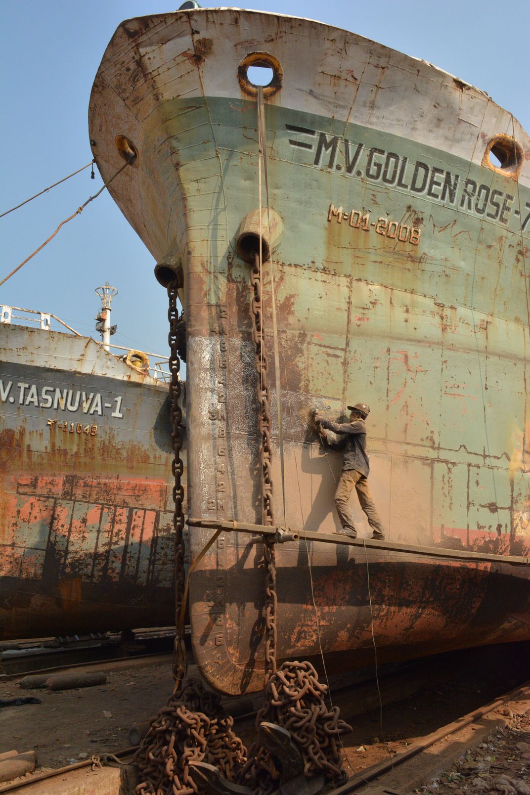 Shipyard worker grinds paint off the hull of a ship. | Smithsonian ...