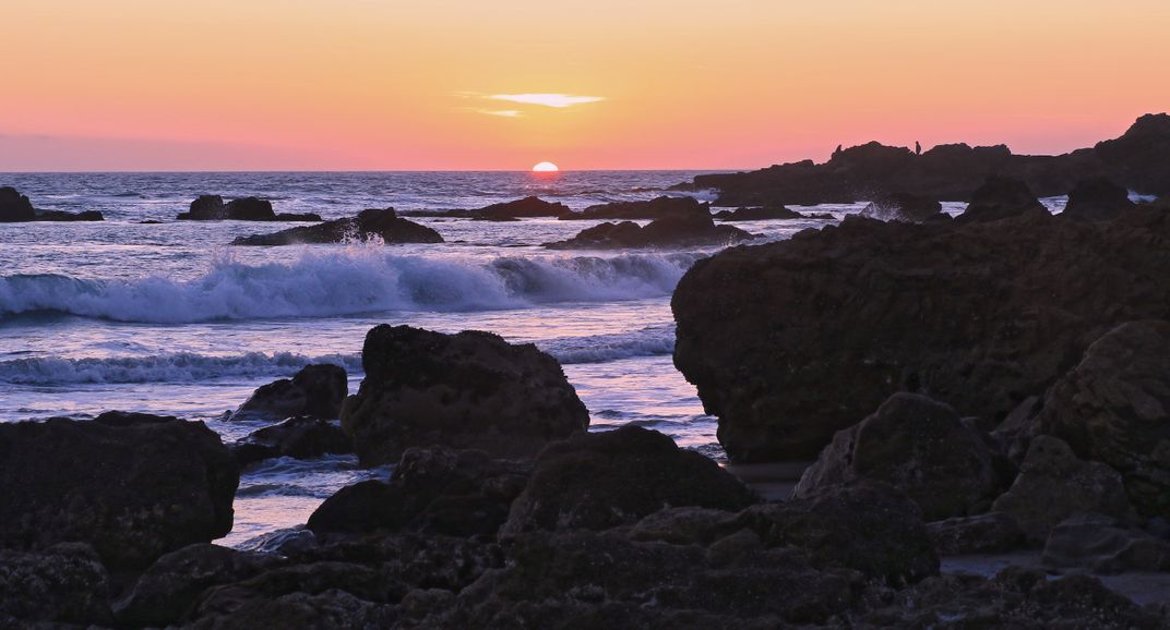 Sun setting over the ocean and people in silhouette exploring on the ...