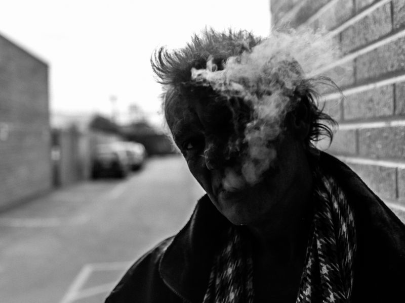 A homeless man smoking in an alley. The slowly rising smoke looks like ...