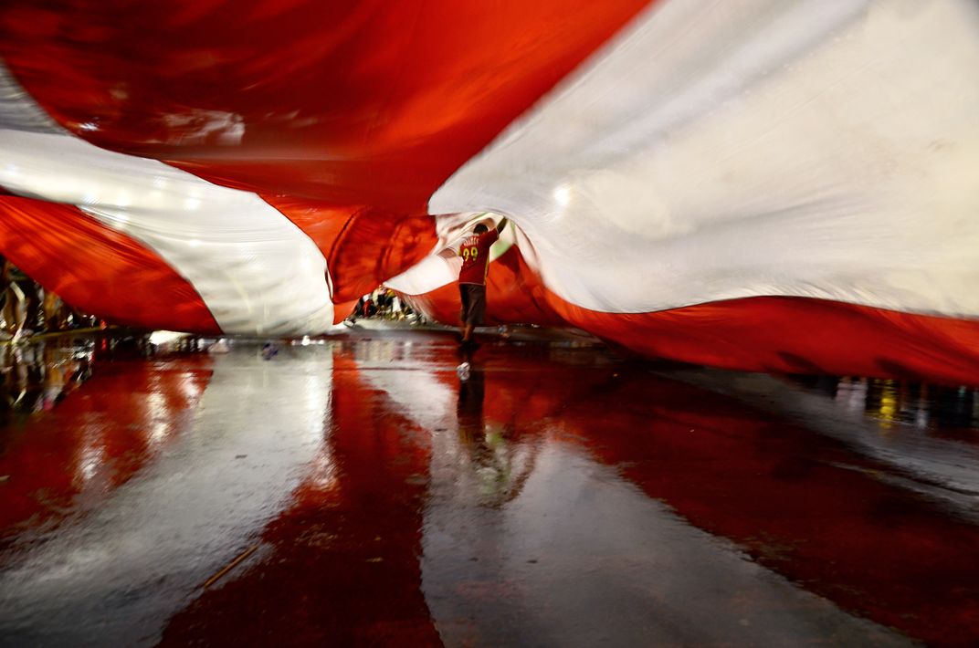 After a rainy afternoon, a man tries to keep dry the flag of his ...