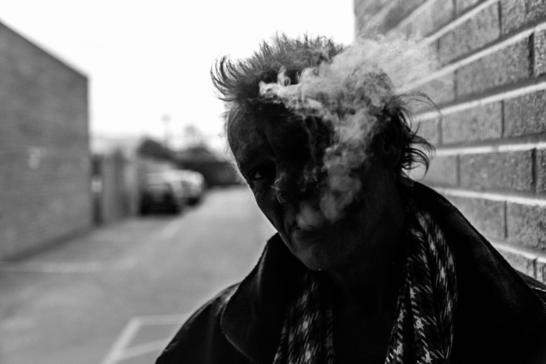 A homeless man smoking in an alley. The slowly rising smoke looks like ...